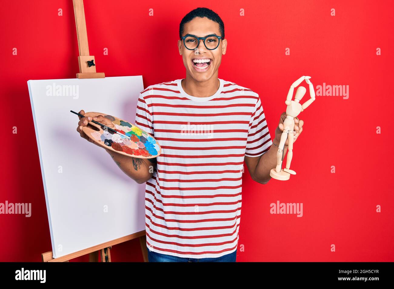 Young african american guy holding painter palette and art manikin ...