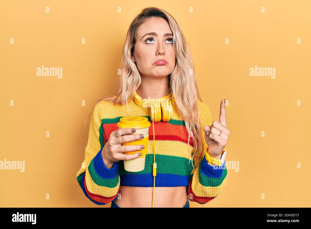 Beautiful young blonde woman drinking cup of coffee wearing headphones ...