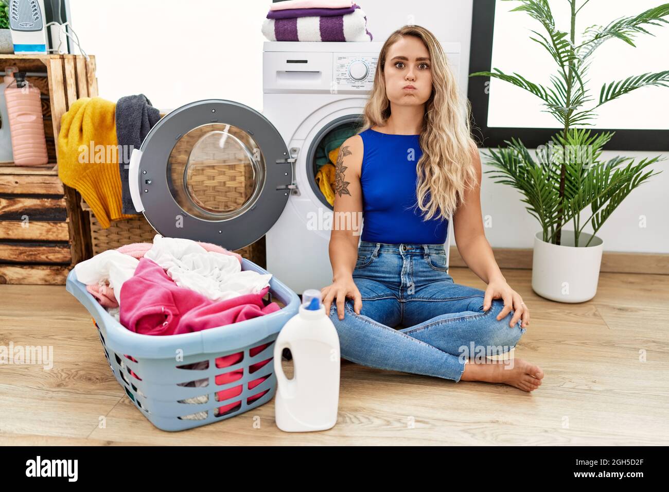 Young beautiful woman doing laundry sitting by wicker basket puffing ...