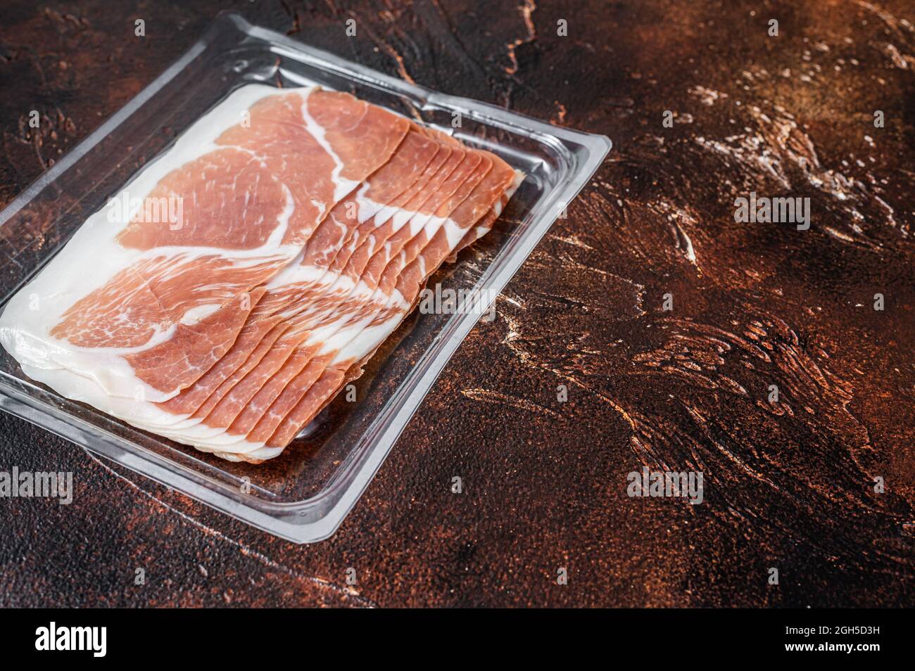 Italian prosciutto crudo or jamon in a vacuum package. Dark background ...
