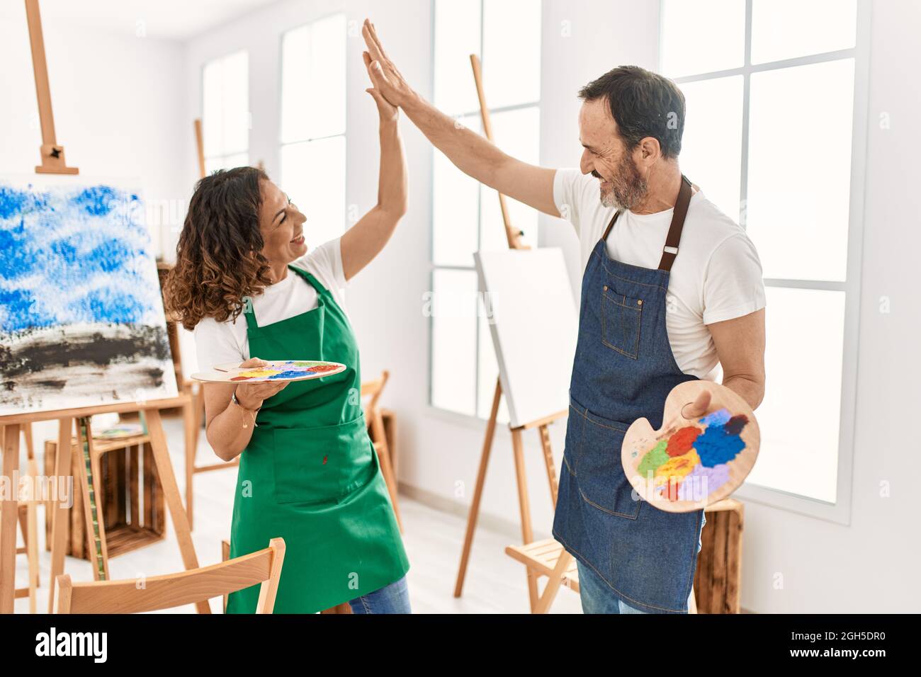 Two middle age student smiling happy holding palette and high five at ...