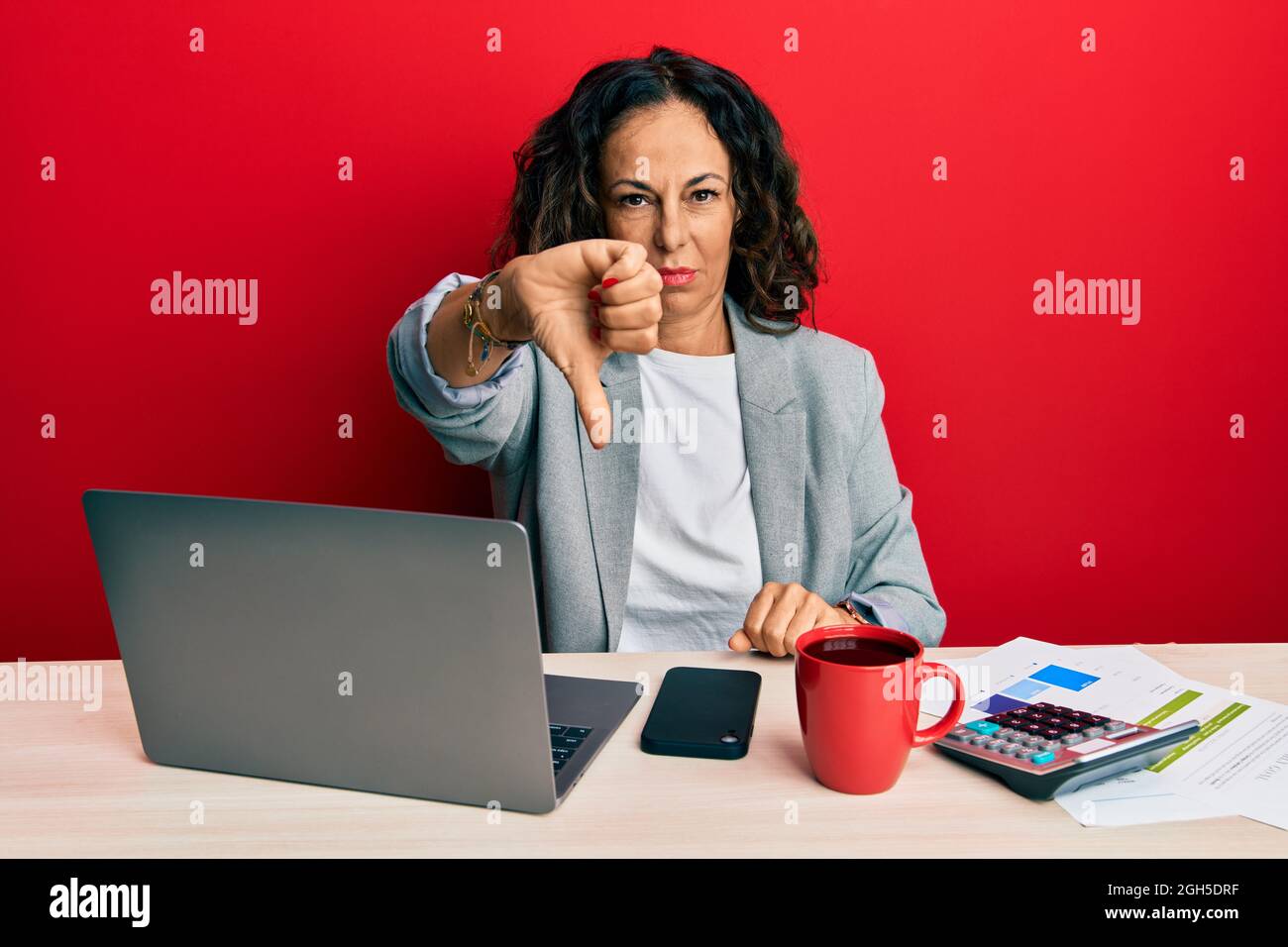 Beautiful middle age woman working at the office drinking a cup of ...