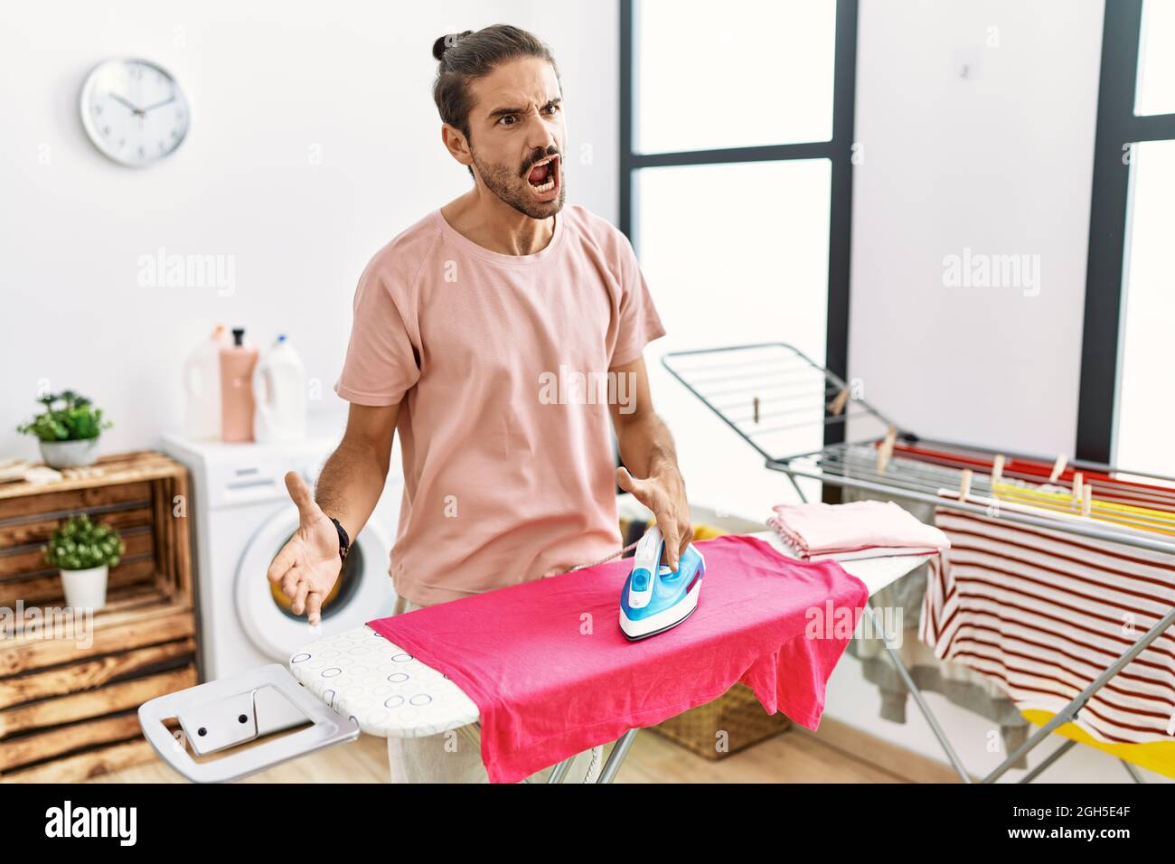 Young hispanic man ironing clothes at home angry and mad screaming ...