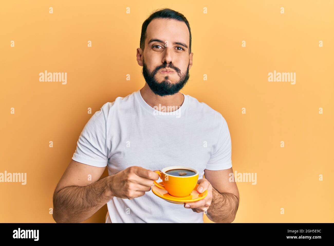Young man with beard drinking a cup coffee puffing cheeks with funny ...