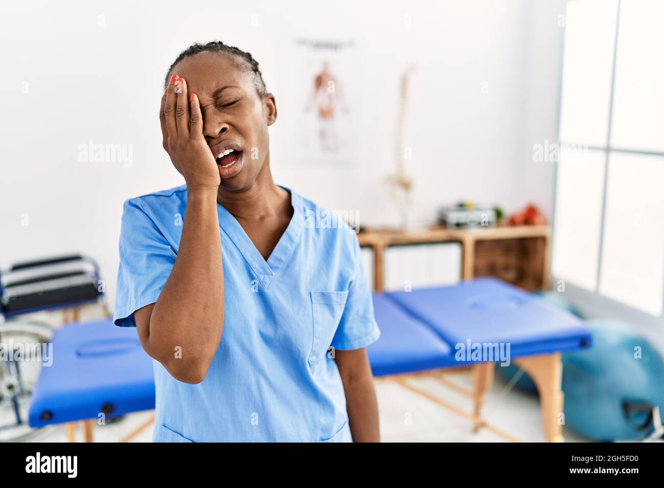 Black woman with braids working at pain recovery clinic yawning tired ...