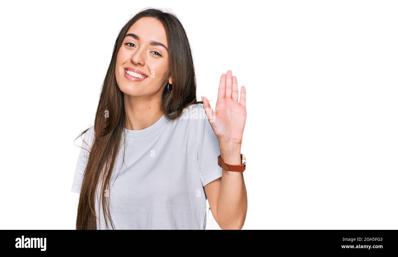 Young hispanic girl wearing casual white t shirt waiving saying hello ...