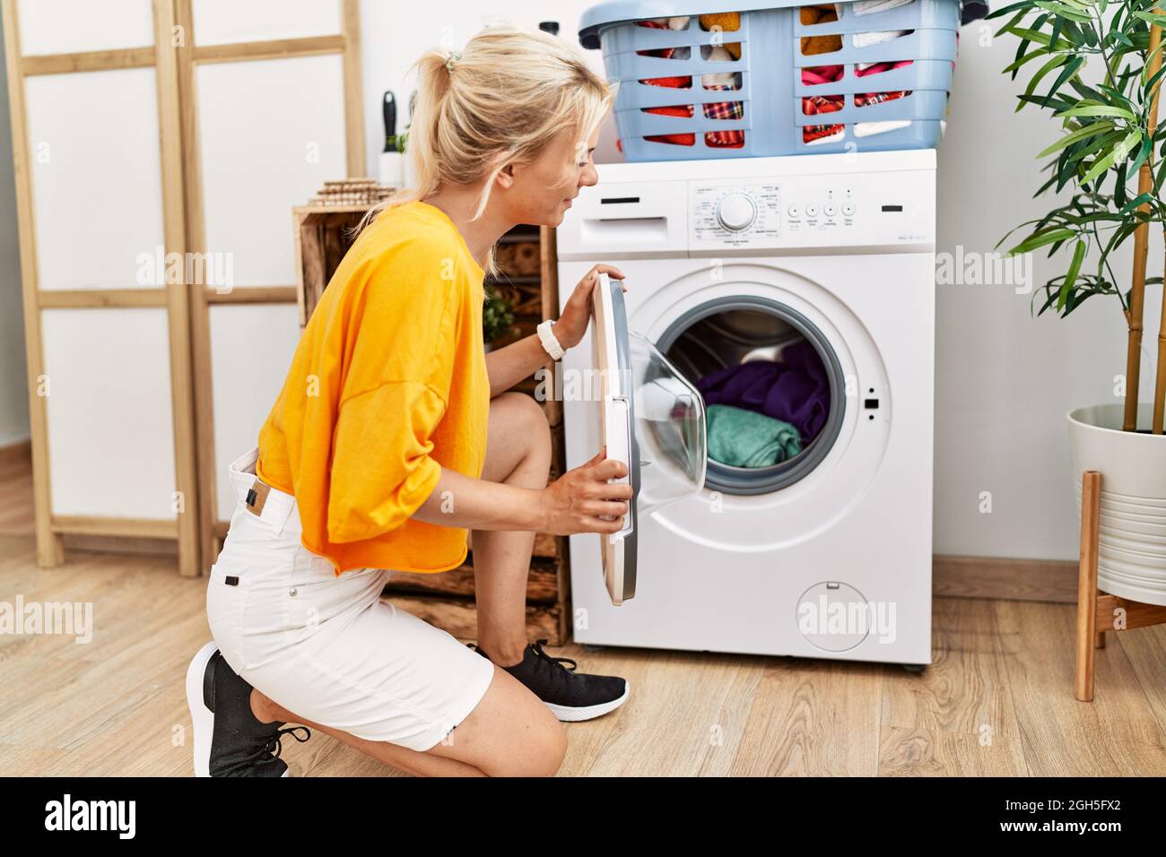 Young blonde girl doing laundry putting clothes into washing machine at home Stock Photo - Alamy