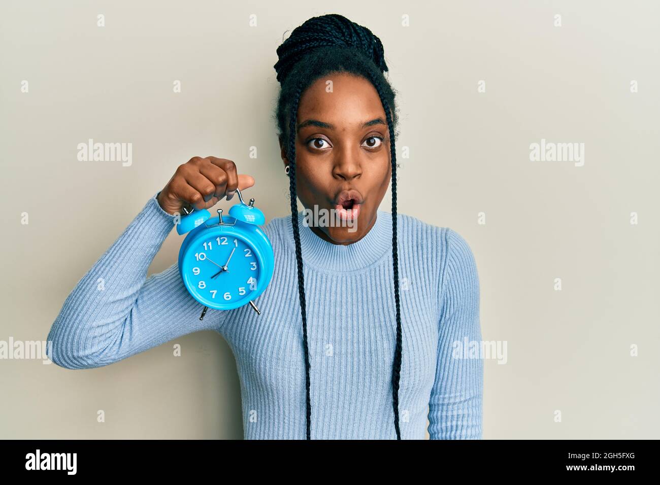 African american woman with braided hair holding alarm clock scared and ...