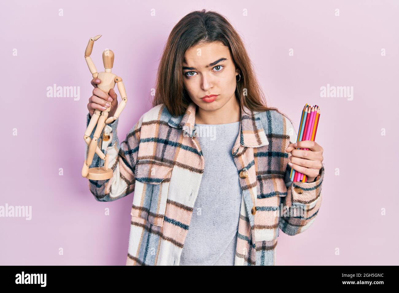 Young caucasian girl holding small wooden manikin and pencils depressed ...
