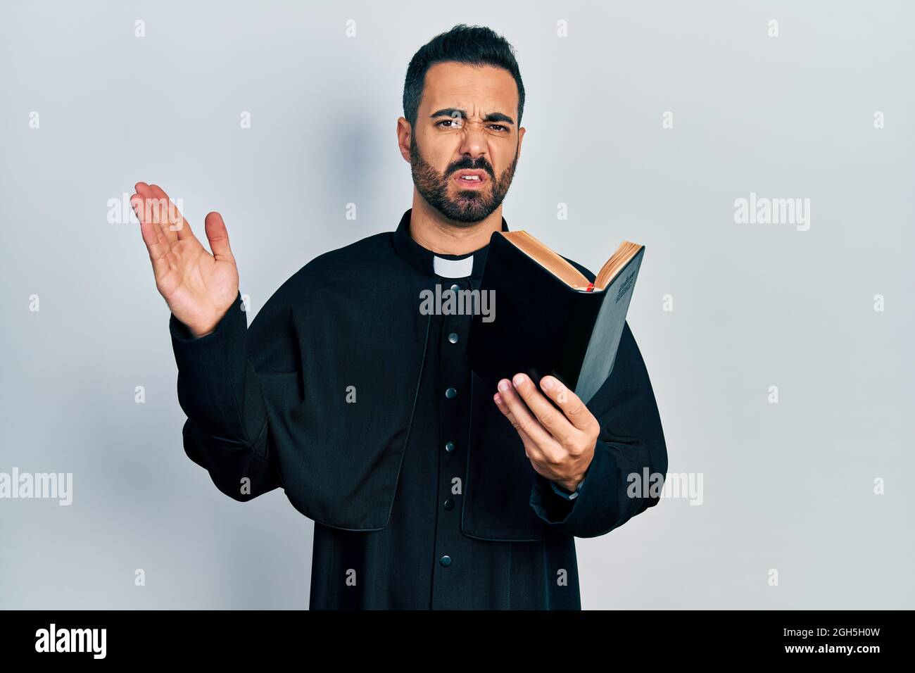 Handsome hispanic priest man with beard holding bible and christian ...
