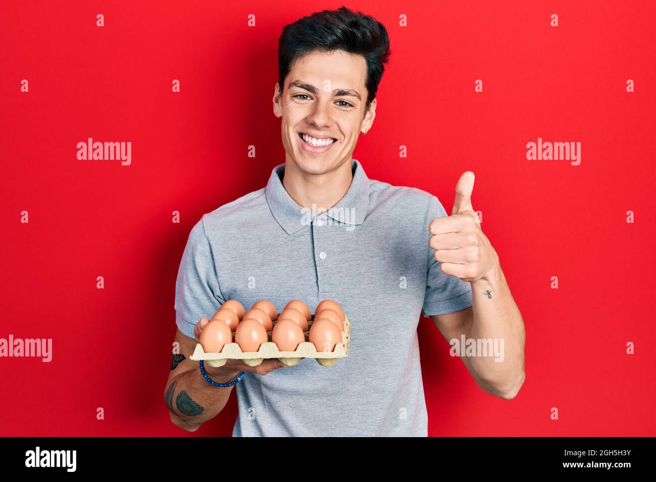 Young hispanic man showing fresh white eggs smiling happy and positive ...