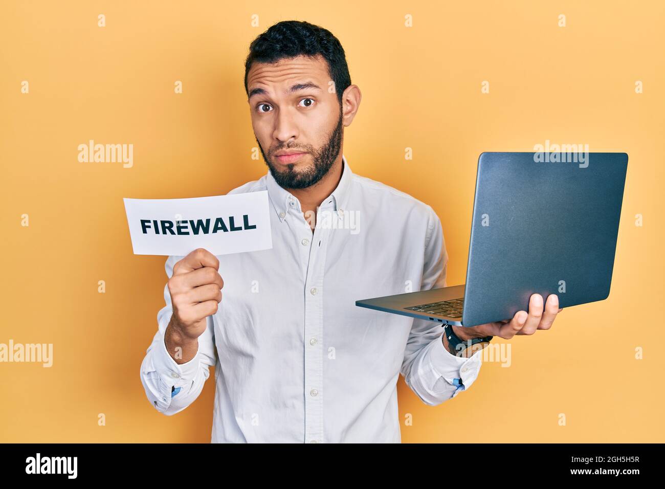 Hispanic man with beard holding computer laptop and firewall banner ...