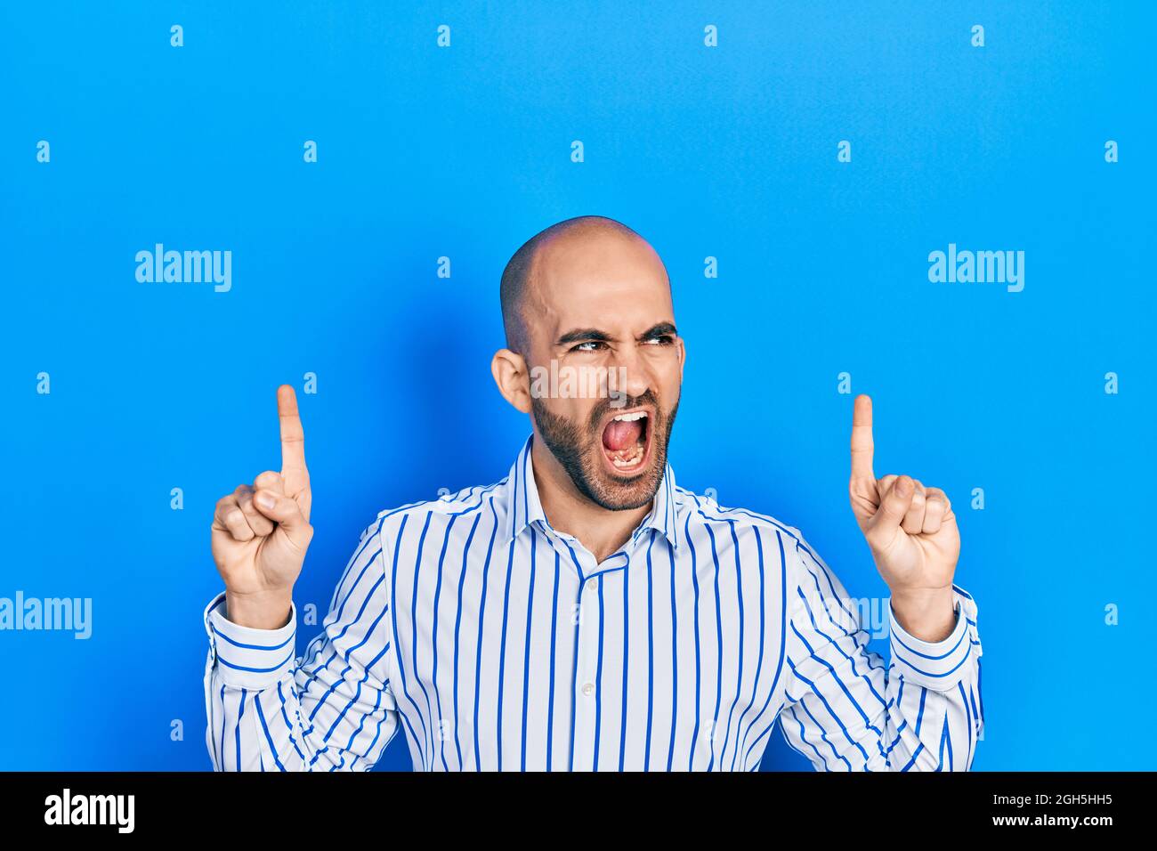 Young bald man pointing up with fingers angry and mad screaming ...