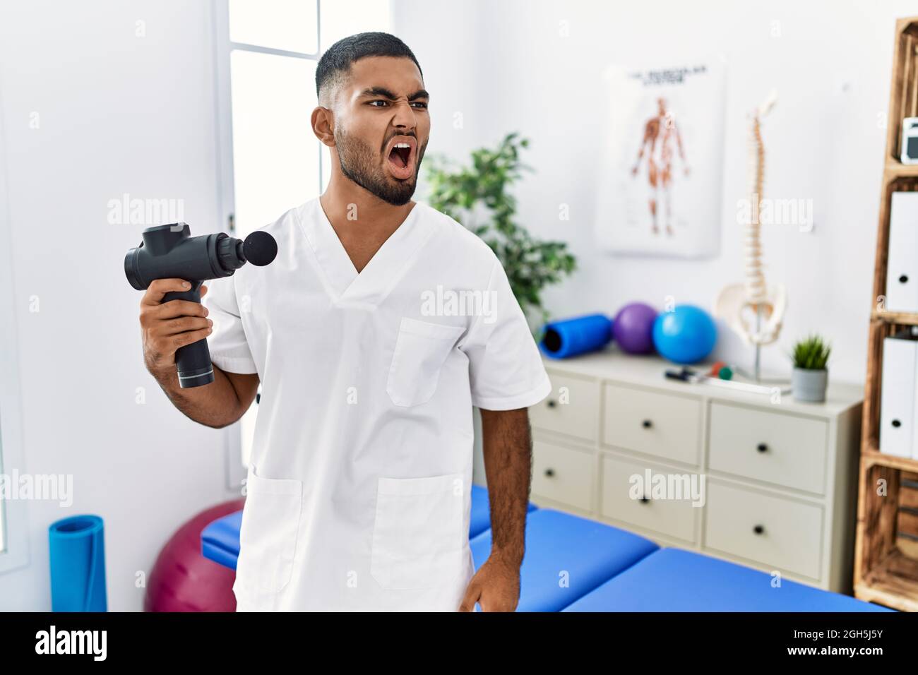 Young indian physiotherapist holding therapy massage gun at wellness ...