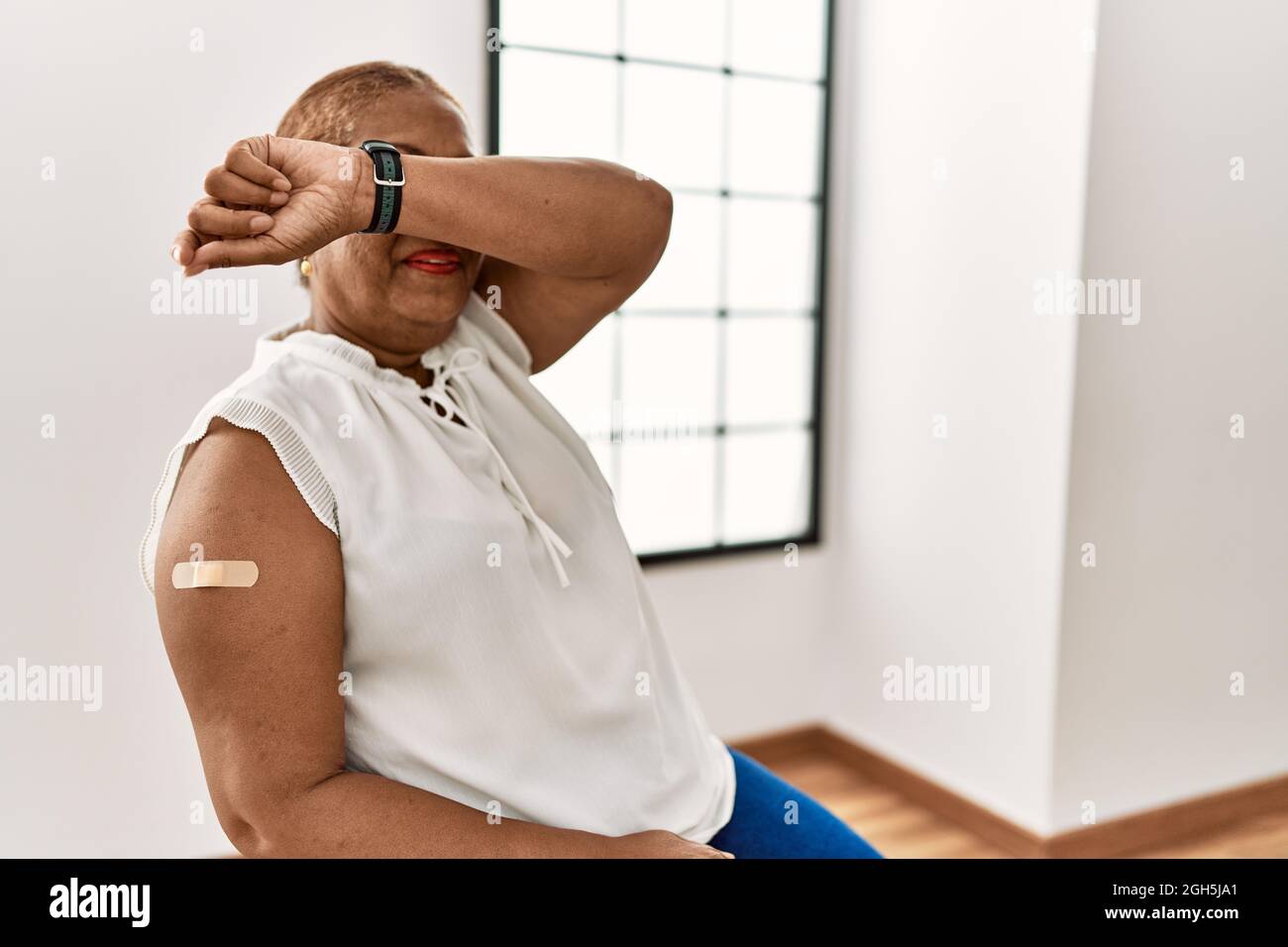 Mature hispanic woman getting vaccine showing arm with band aid smiling ...