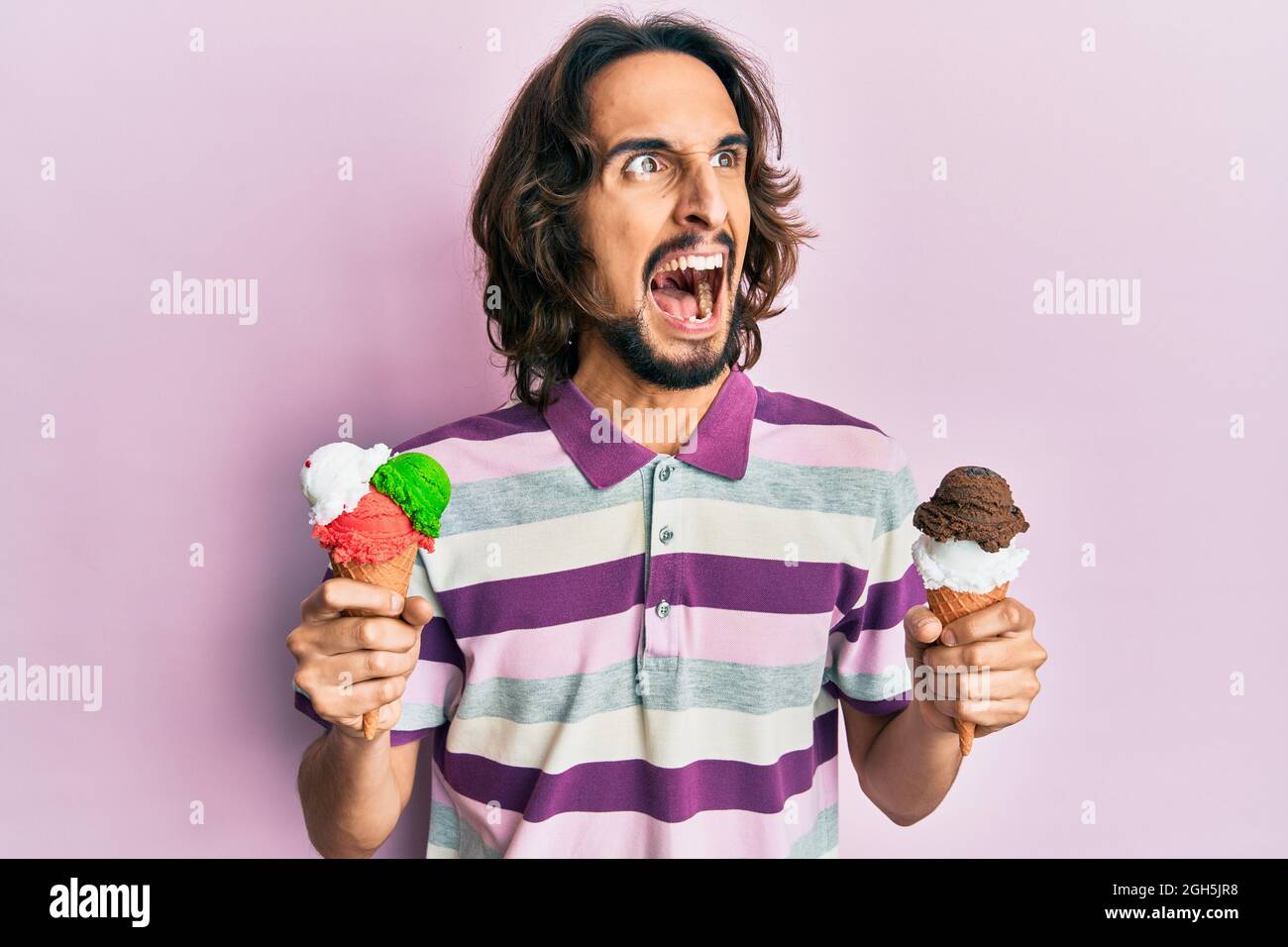 Young hispanic man holding ice cream angry and mad screaming frustrated ...