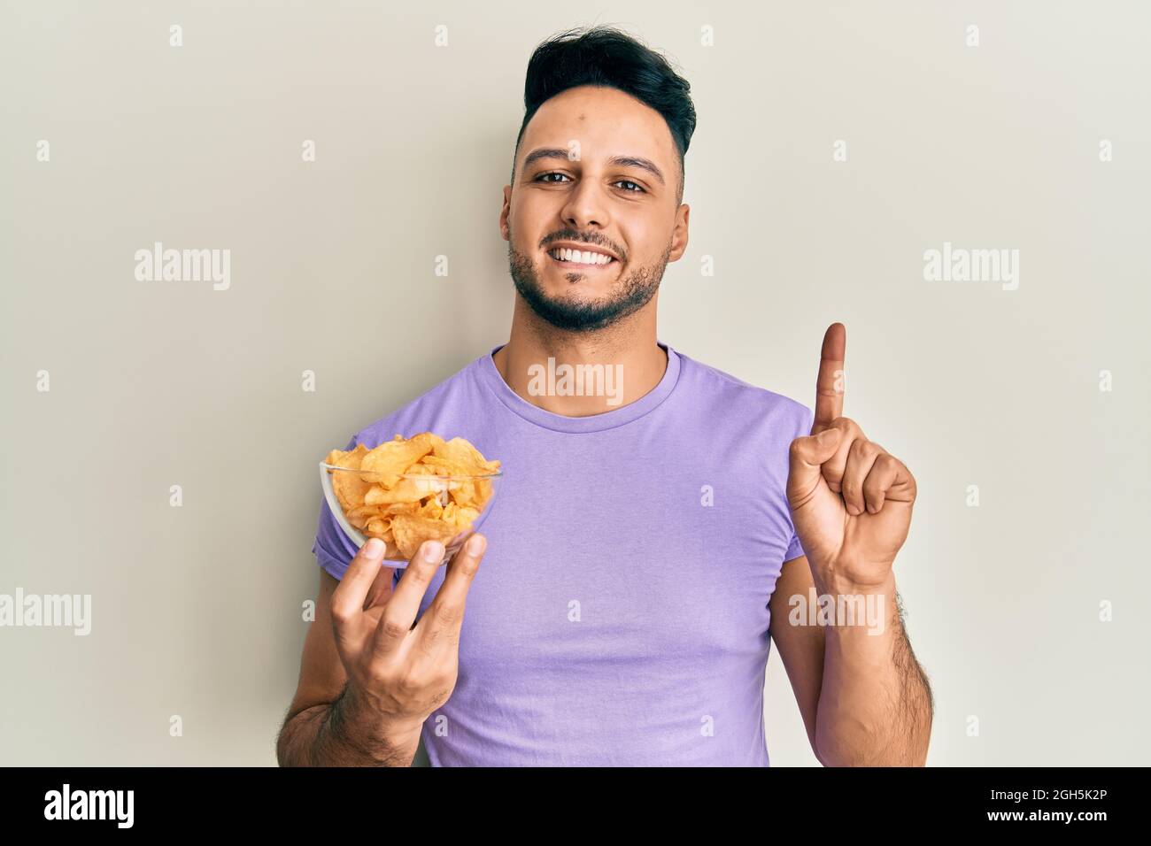 Young arab man holding potato chip smiling with an idea or question ...