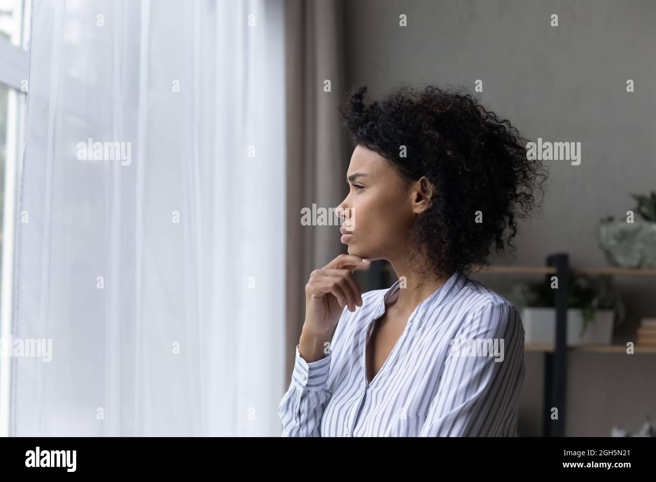 Contemplative young black businesswoman look at window touch chin ...