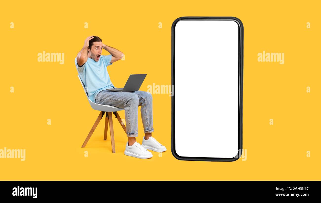 Surprised shocked guy using laptop, empty phone screen Stock Photo - Alamy