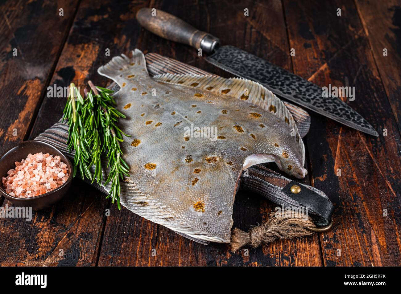 Raw plaice flatfish fish on butcher board with knife. Dark wooden ...