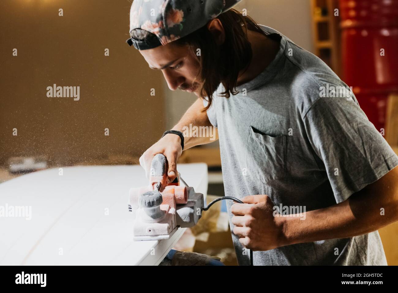 Male shaper using electric planer and polishing surface of surfboard in ...