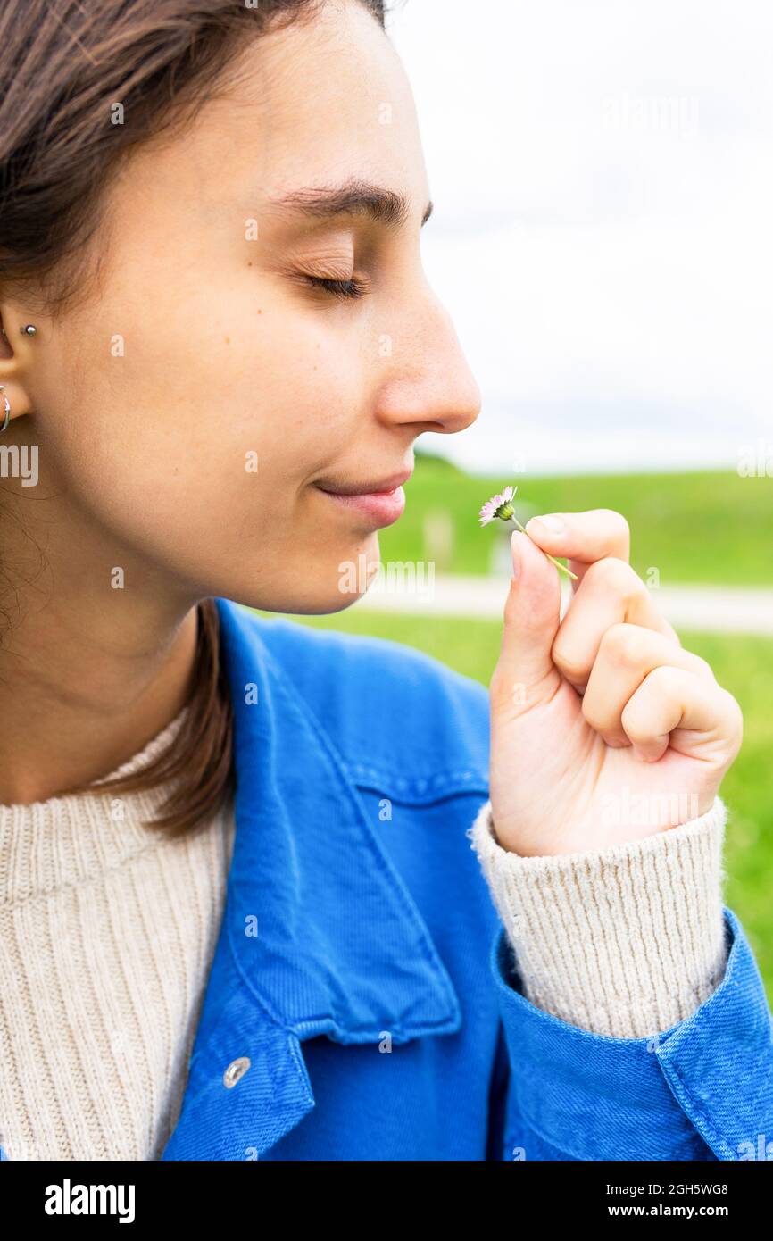 Gentle female with closed eyes sniffing aroma of small flower in park ...