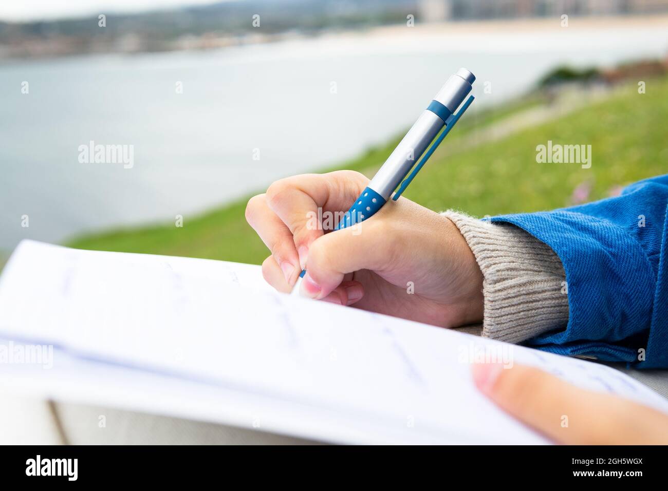Anonymous female writing with a blue pen in a notepad while near sea ...