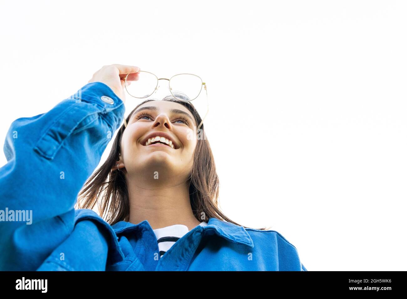 Low angle of delighted female with eyeglasses and in blue denim jacket ...