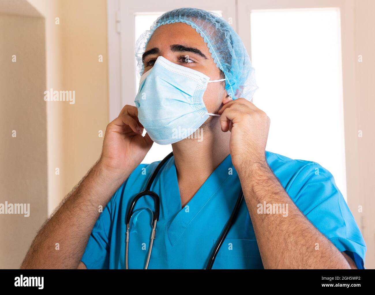 Side view of male medic in uniform putting on disposable mask during ...