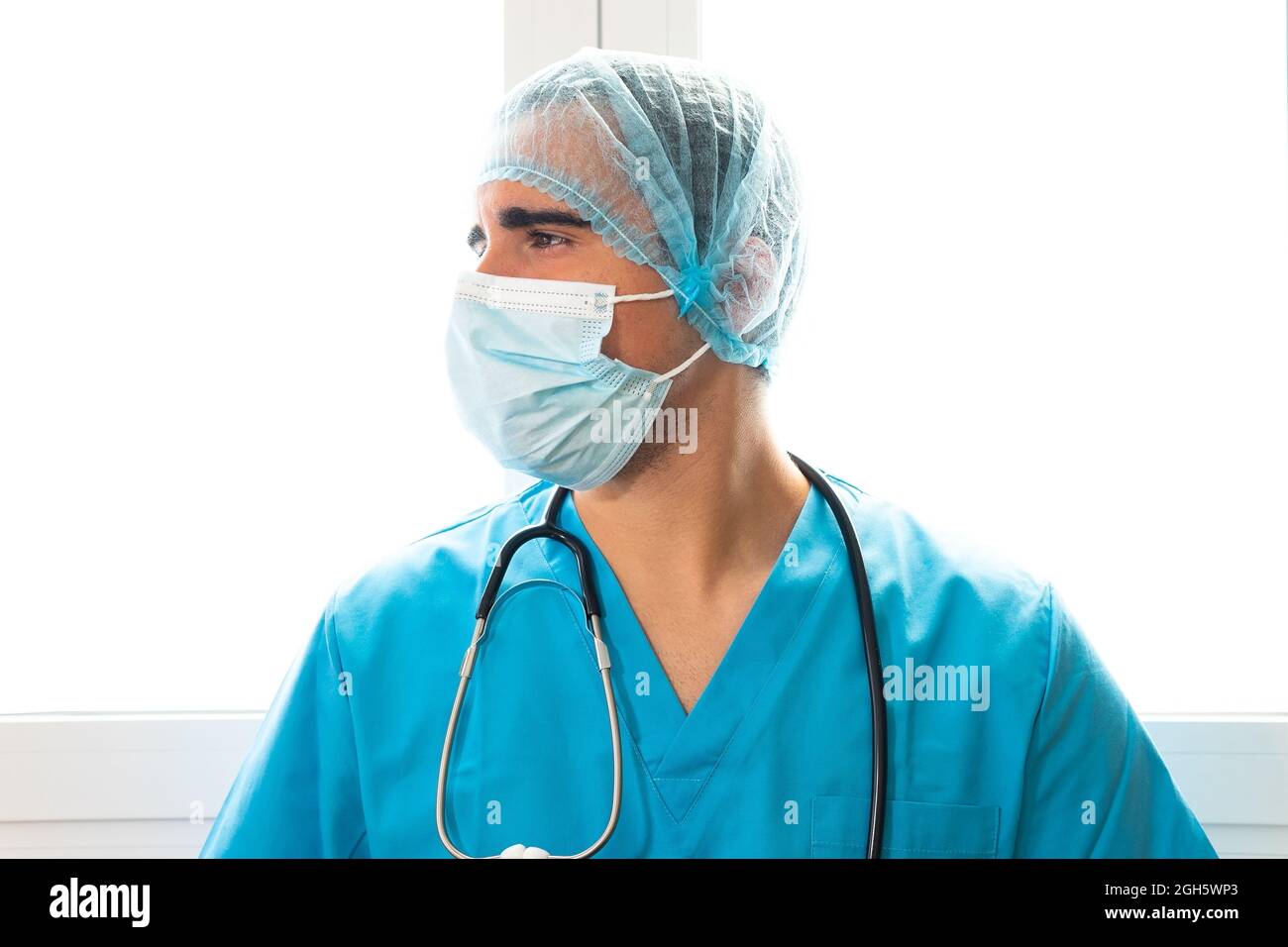 Side view of male medic in mask and uniform standing near window in ...