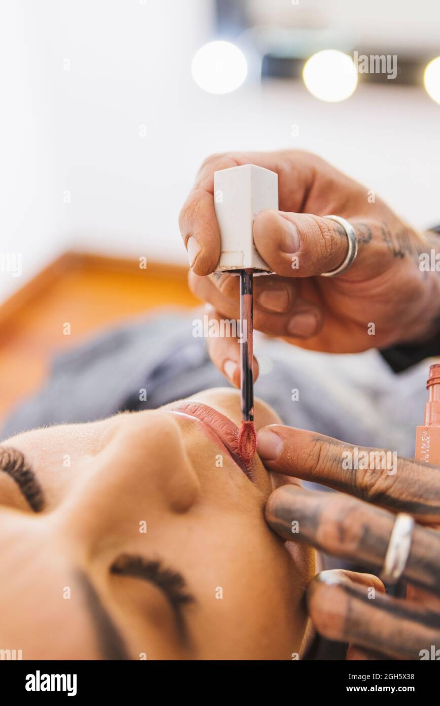 Cheerful blond Woman with closed eyes while tattooed makeup artist ...