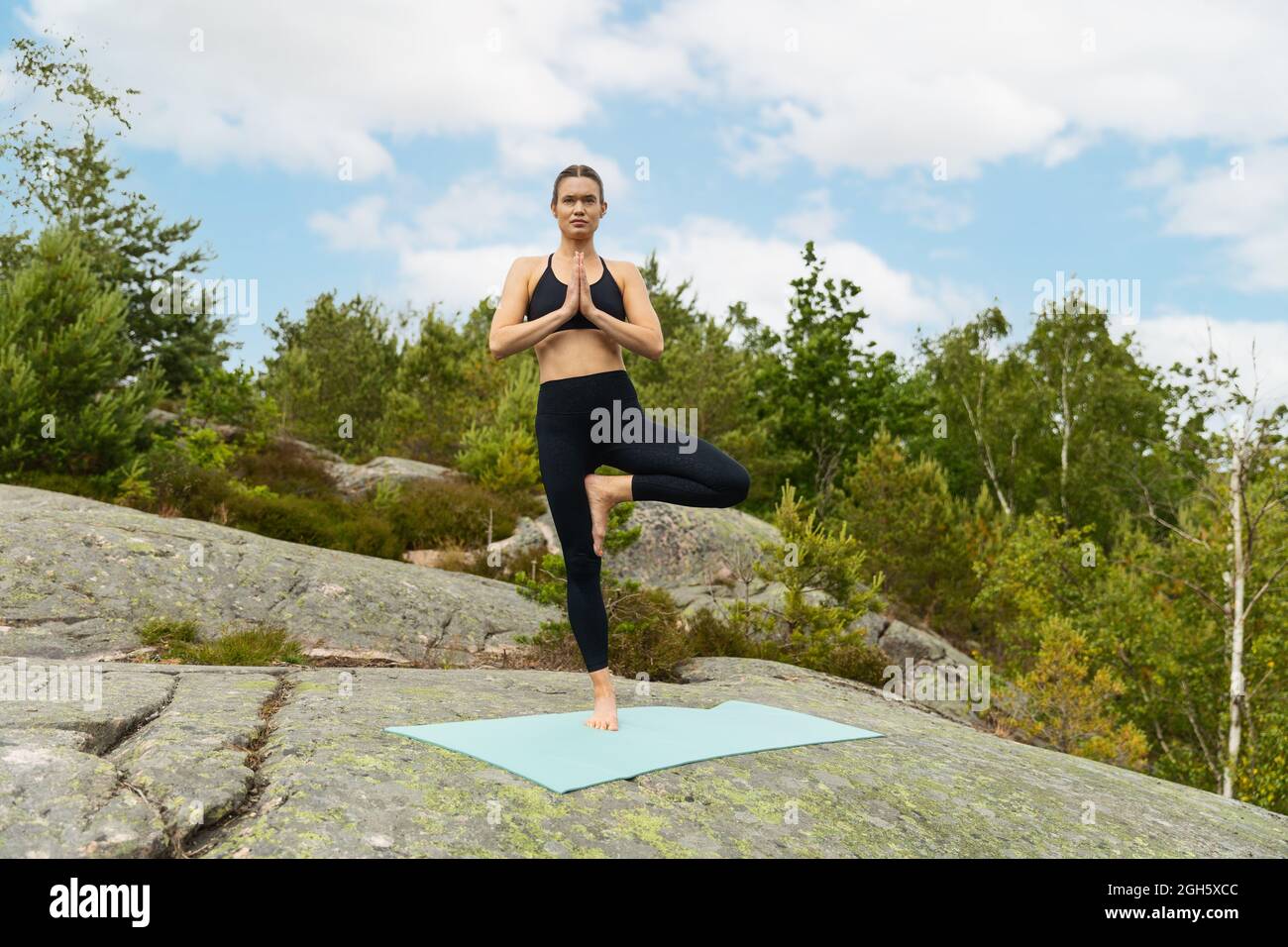 Full body barefoot female doing Tree pose on mat while practicing yoga ...