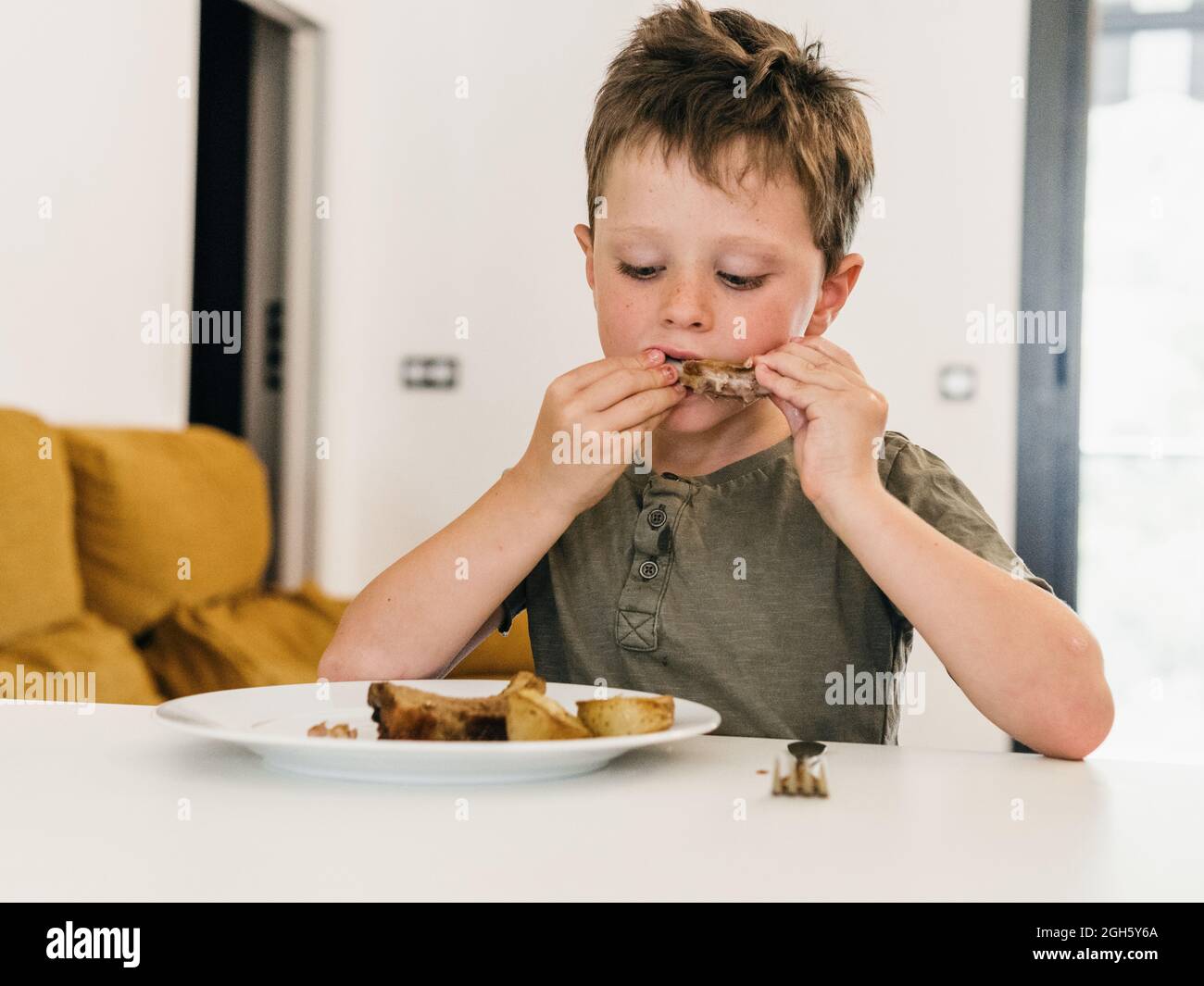 Adorable kid eating appetizing pork ribs during lunch at home and ...