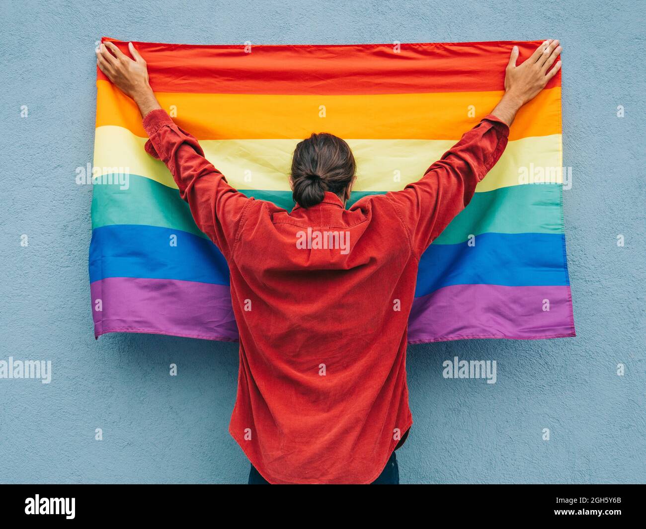 Back view of anonymous homosexual male standing with LGBT rainbow flag ...