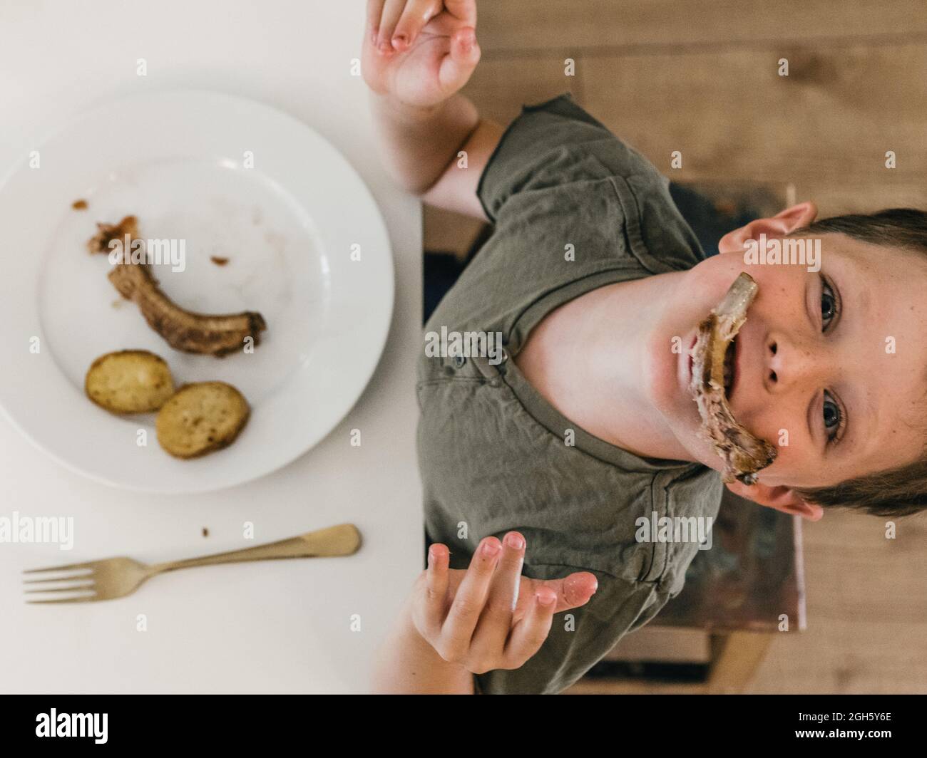 Top view of playful child with pork rib in mouth having lunch at table ...