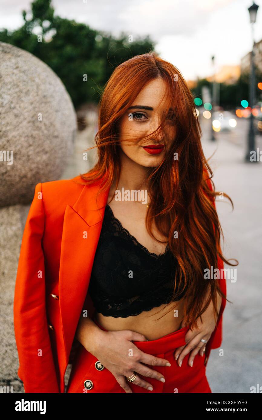 Charming female with long red hair and in trendy orange suit standing ...