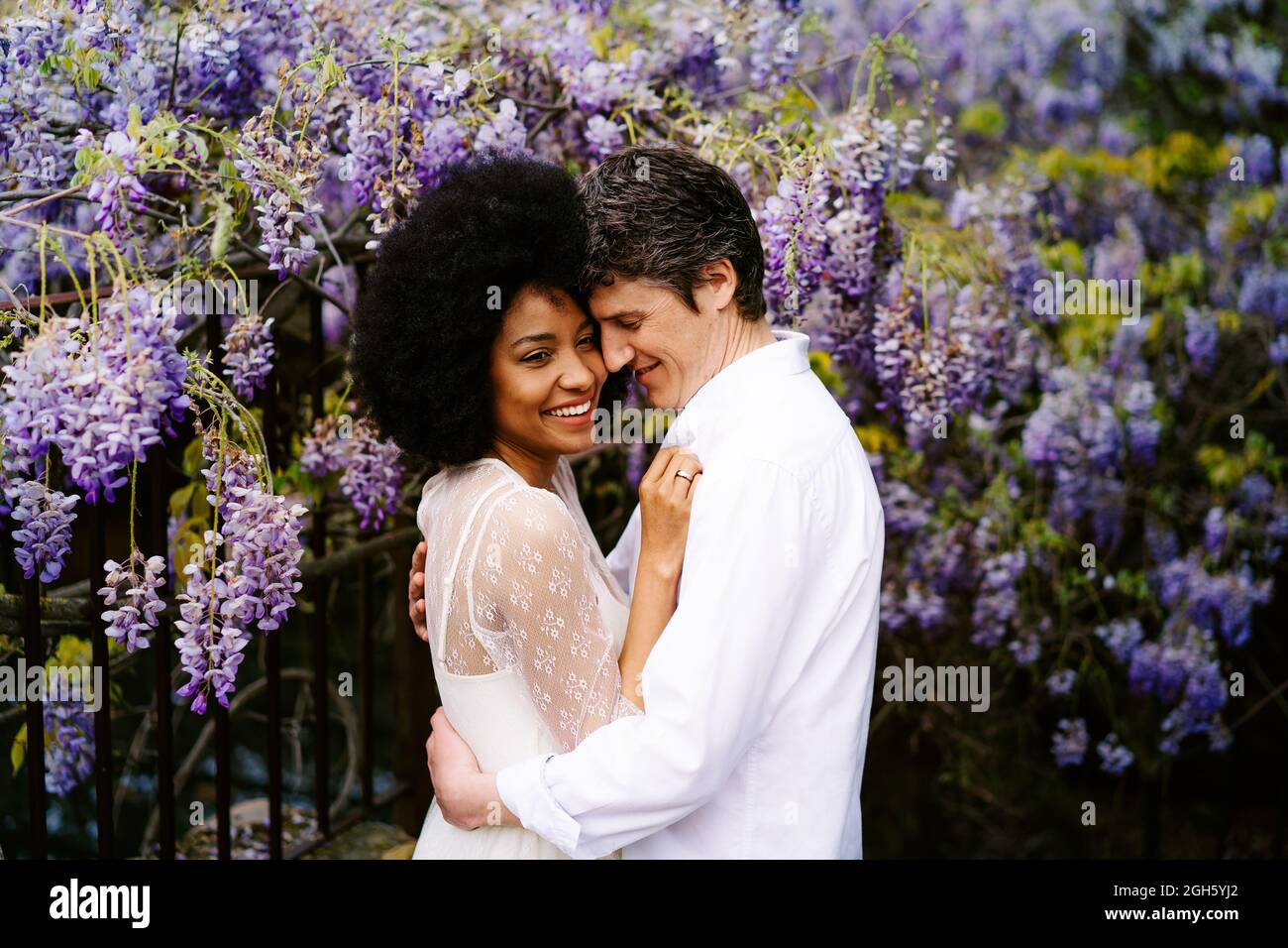 Side view of loving multiracial couple embracing in park with blooming ...