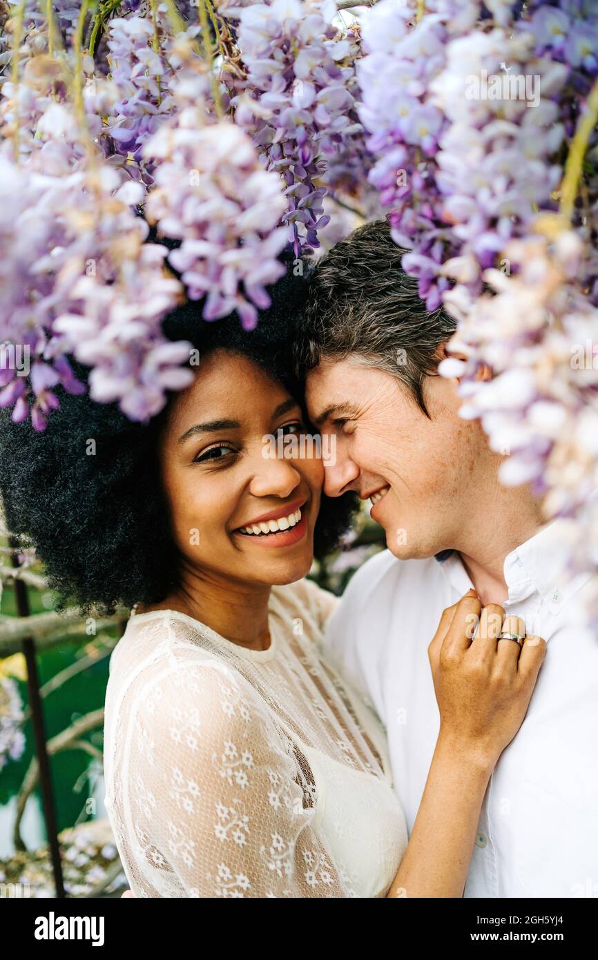 Side view of loving multiracial couple embracing in park with blooming ...