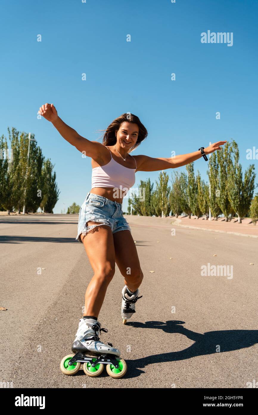 Side view of fit cheerful female in rollerblades showing stunt on road ...