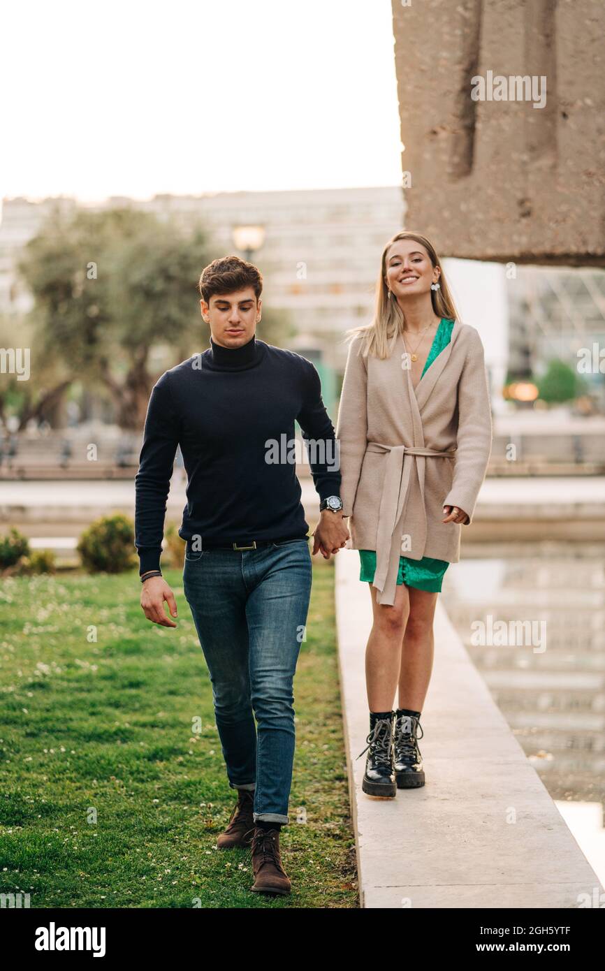 Stylish couple in love holding hands and walking in city while enjoying ...