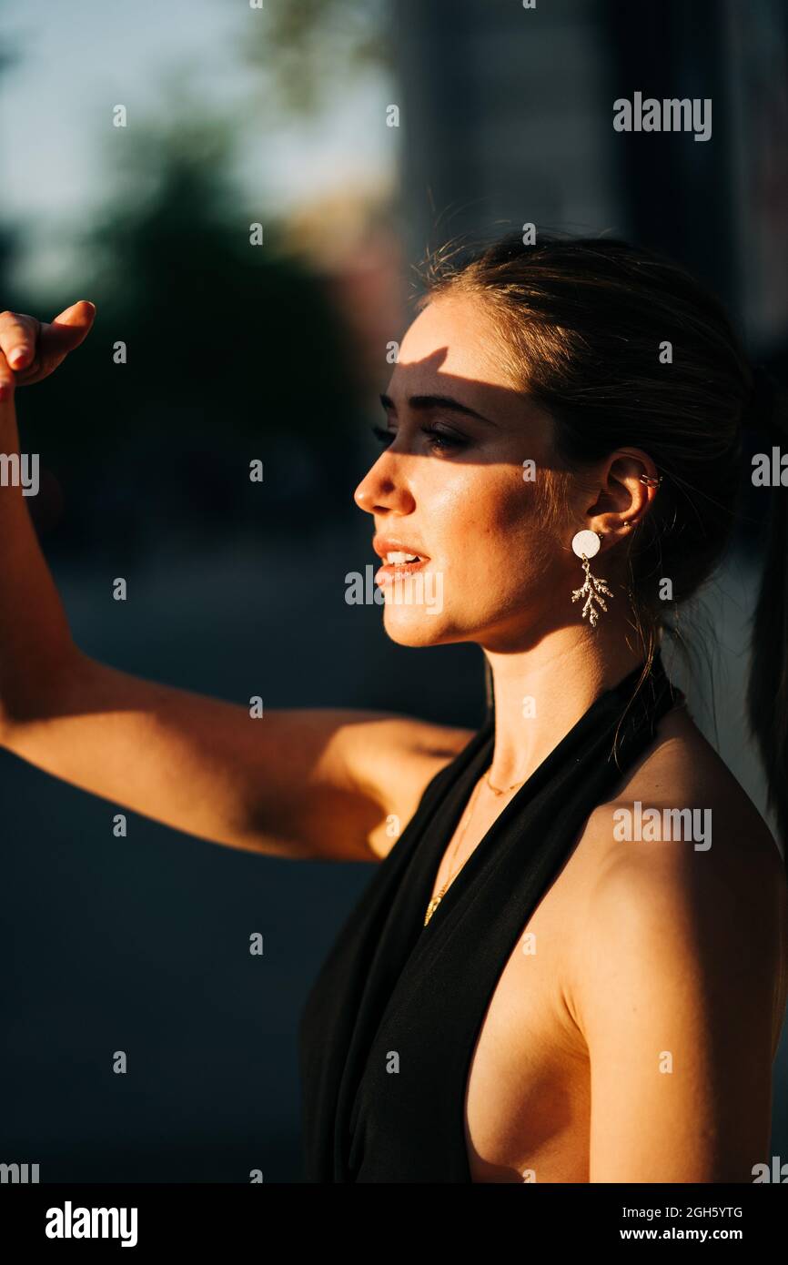 Side view of trendy female covering face from sunlight while standing ...