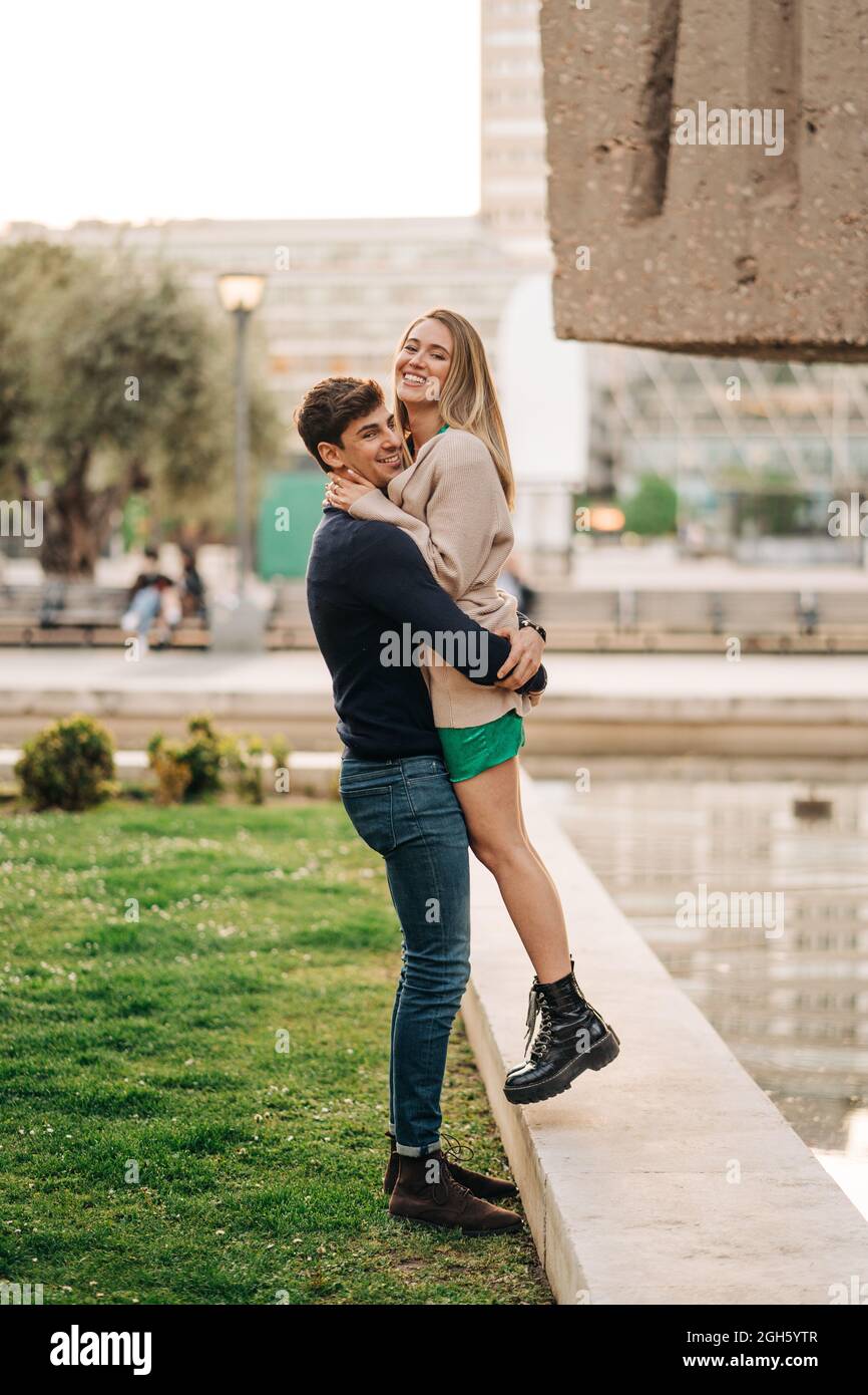 Side view of loving boyfriend lifting stylish girlfriend in city street ...