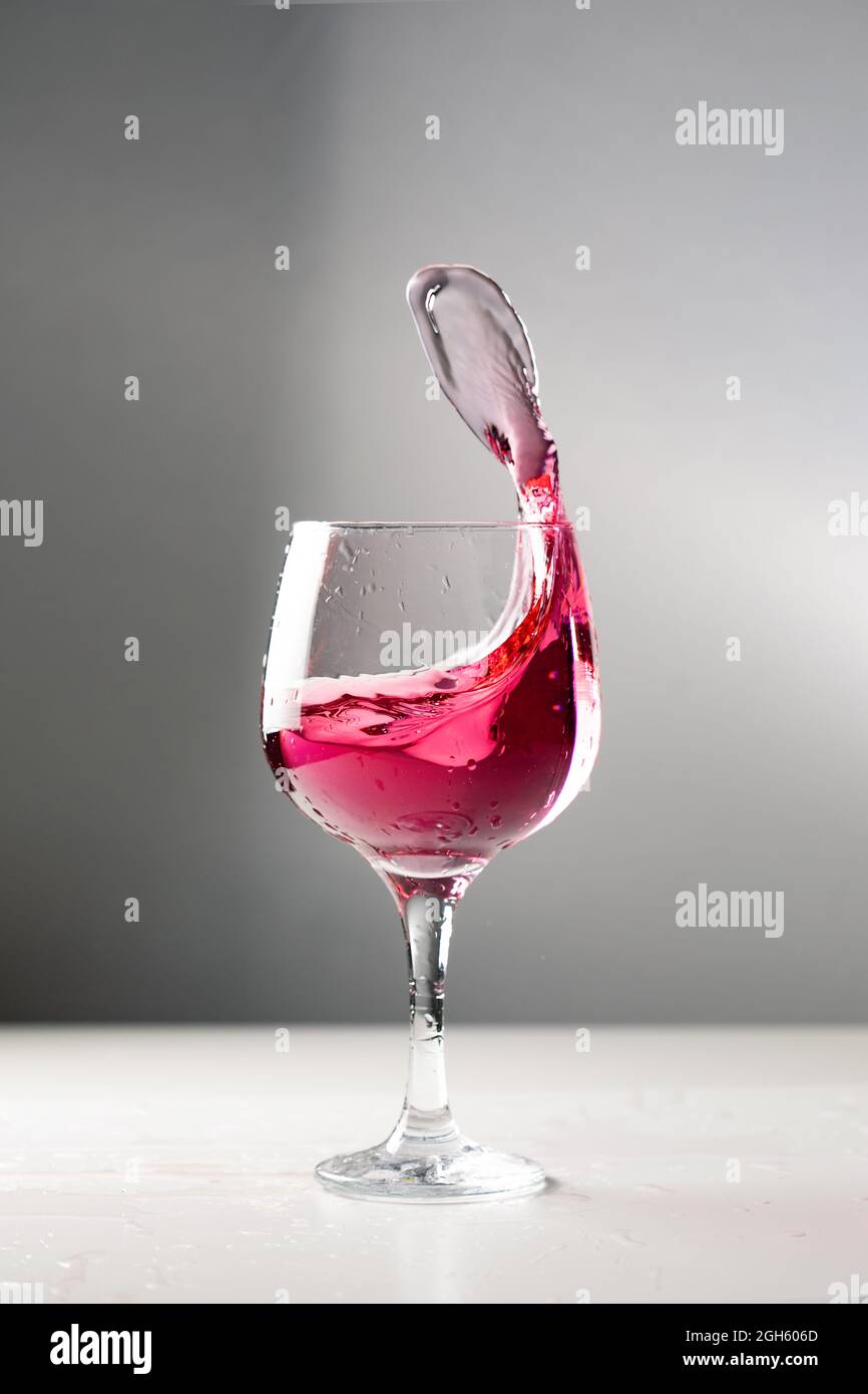 Cold alcohol red drink splashing out of glass goblet on grey background ...