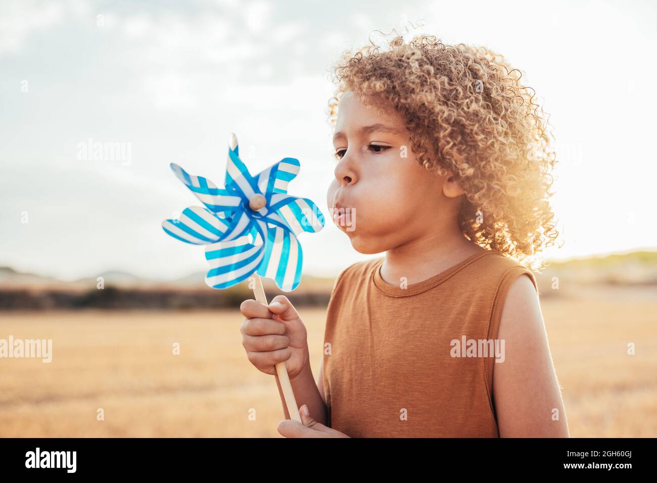 Ethnic kid with curly hair blowing on pinwheel while playing in field ...