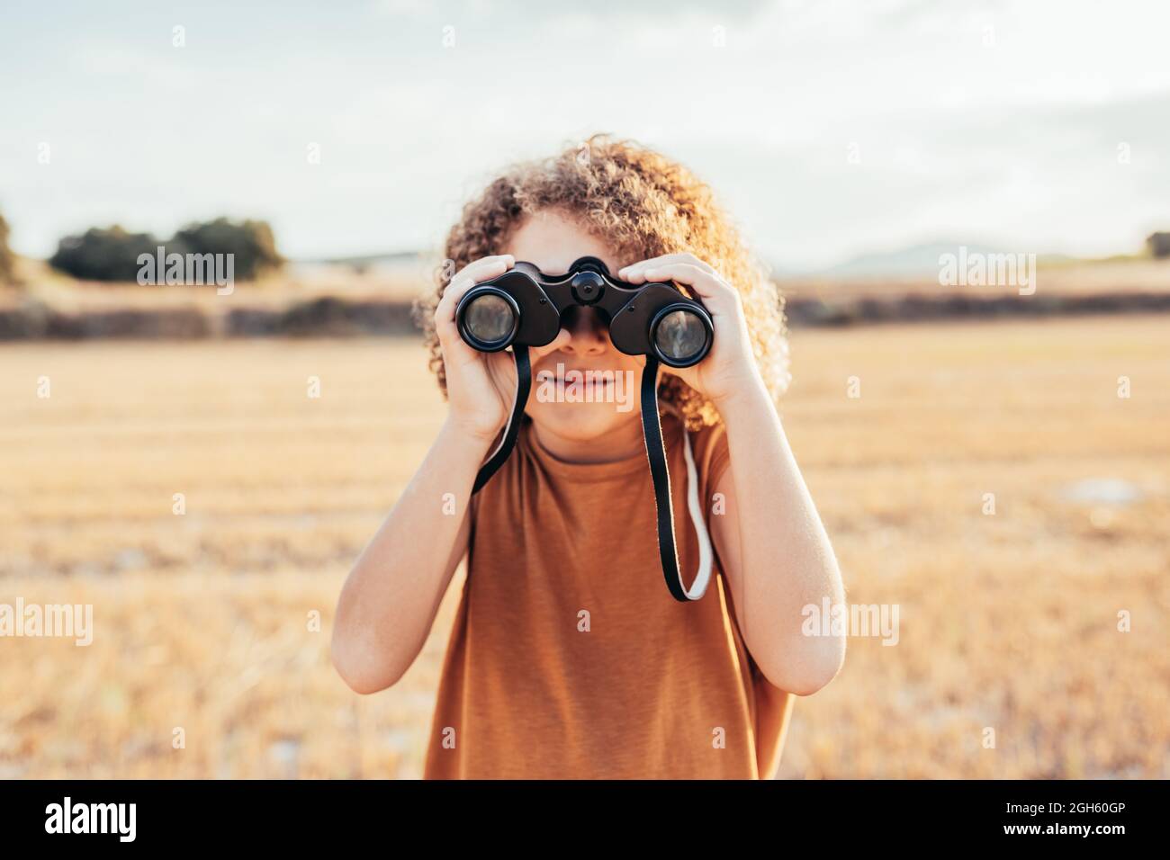 Delighted ethnic child with Afro hairstyle looking through binoculars ...