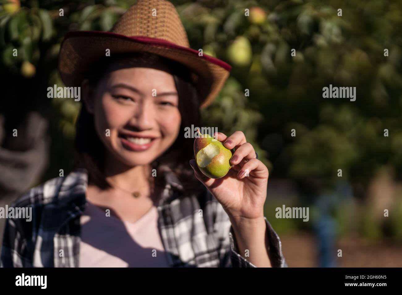 Delighted ethnic female farmer standing with ripe bitten pear in summer ...