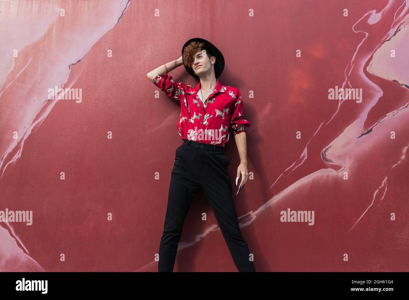 Young vain man in stylish wear standing on tiled walkway while looking ...