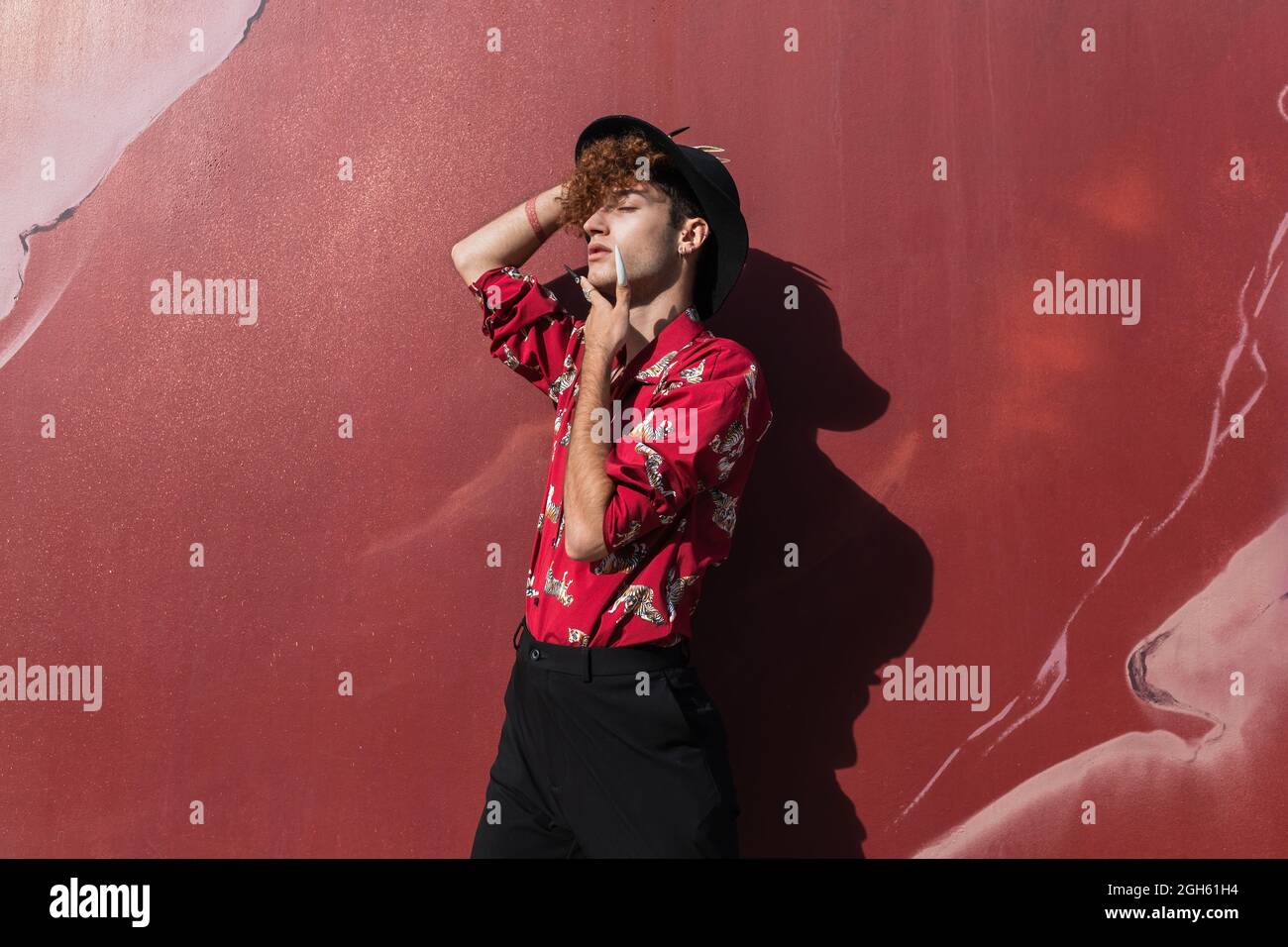 Young vain man in stylish wear standing on tiled walkway with eyes ...