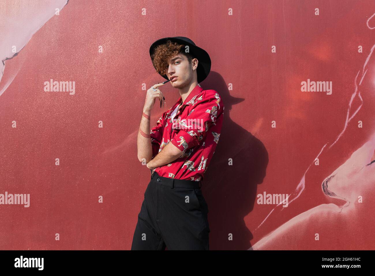 Young vain man in stylish wear standing on tiled walkway while looking ...