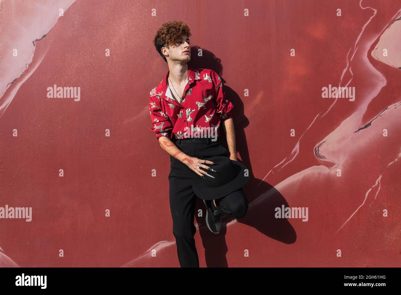 Young vain man with long nails in stylish wear standing on tiled ...